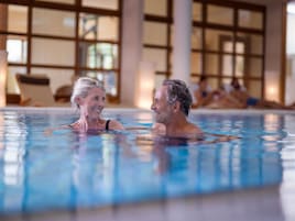 Uma piscina com água cristalina, rodeada por amplas janelas e áreas de estar internas.