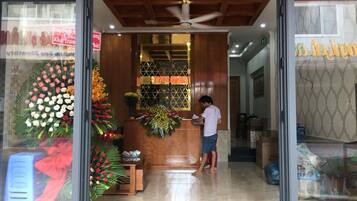 Bancada de recepção com um homem em frente, um arranjo floral grande e uma placa sobre a entrada.