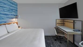 Quarto de hotel com uma cama, uma escrivaninha, uma cadeira, televisão de tela plana e um quadro na parede.