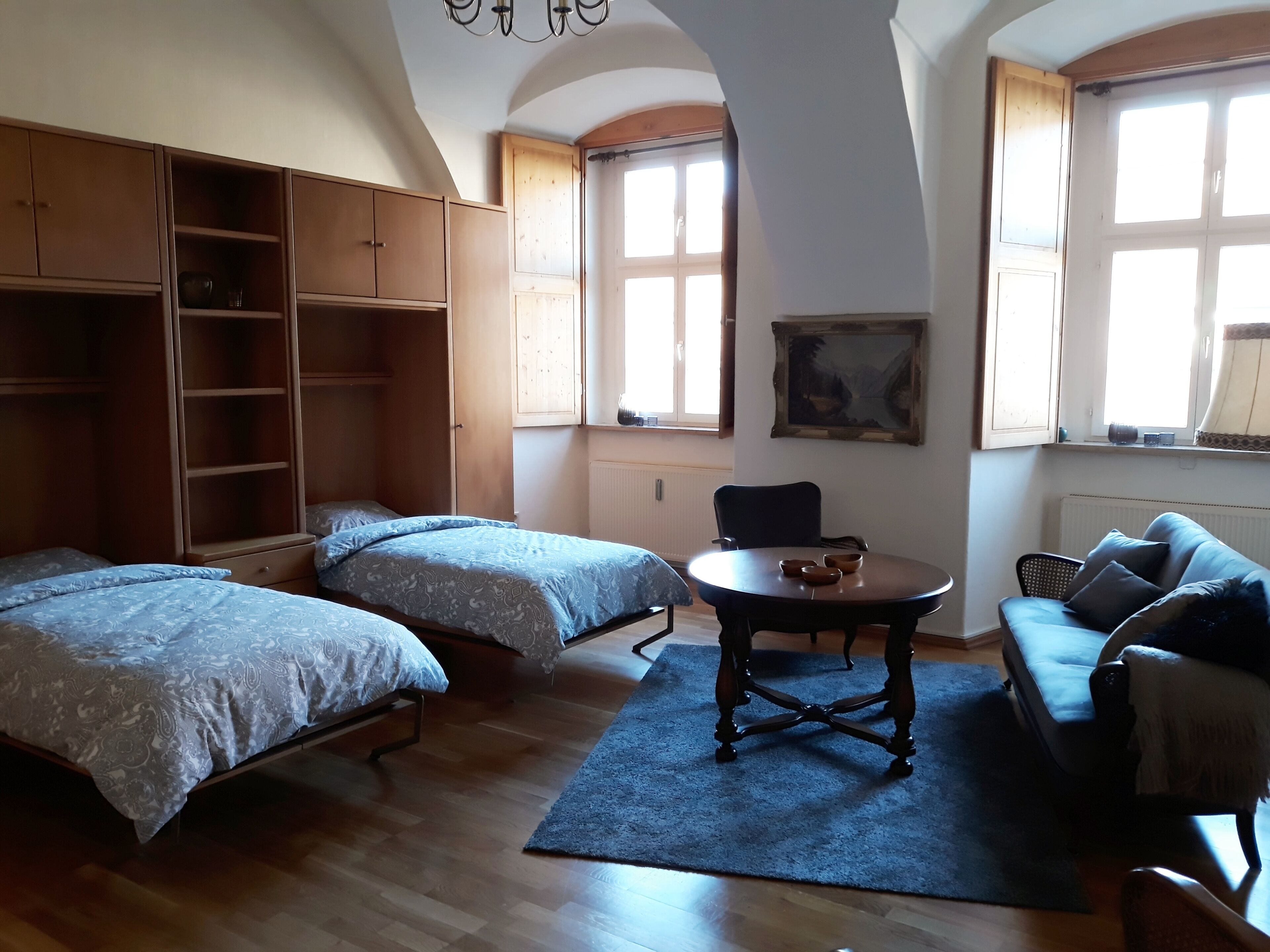 Quarto com duas camas de solteiro, um guarda-roupa de madeira, uma mesa de jantar com cadeiras, um sofá e um quadro na parede.
