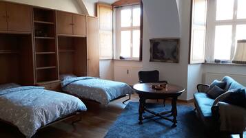 Quarto com duas camas de solteiro, um guarda-roupa de madeira, uma mesa de jantar com cadeiras, um sofá e um quadro na parede.