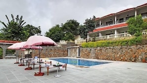 Uma área de piscina com espreguiçadeiras e guarda-sóis, um muro de pedra e um edifício com telhado vermelho.