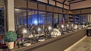Disposição de buffet com várias estações de serviço, incluindo expositores de comida tampados e uma variedade de pratos.