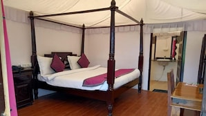 Uma cama de dossel com estrutura de madeira e roupa de cama branca, um criado-mudo de madeira com abajur e uma cadeira de madeira.