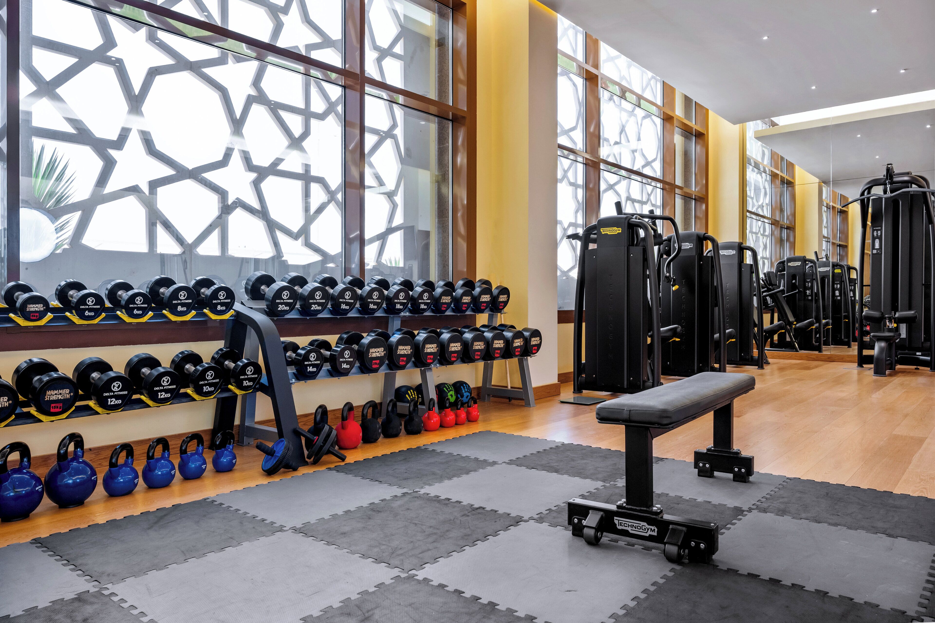 Academia com equipamentos de musculação, kettlebells e um banco.