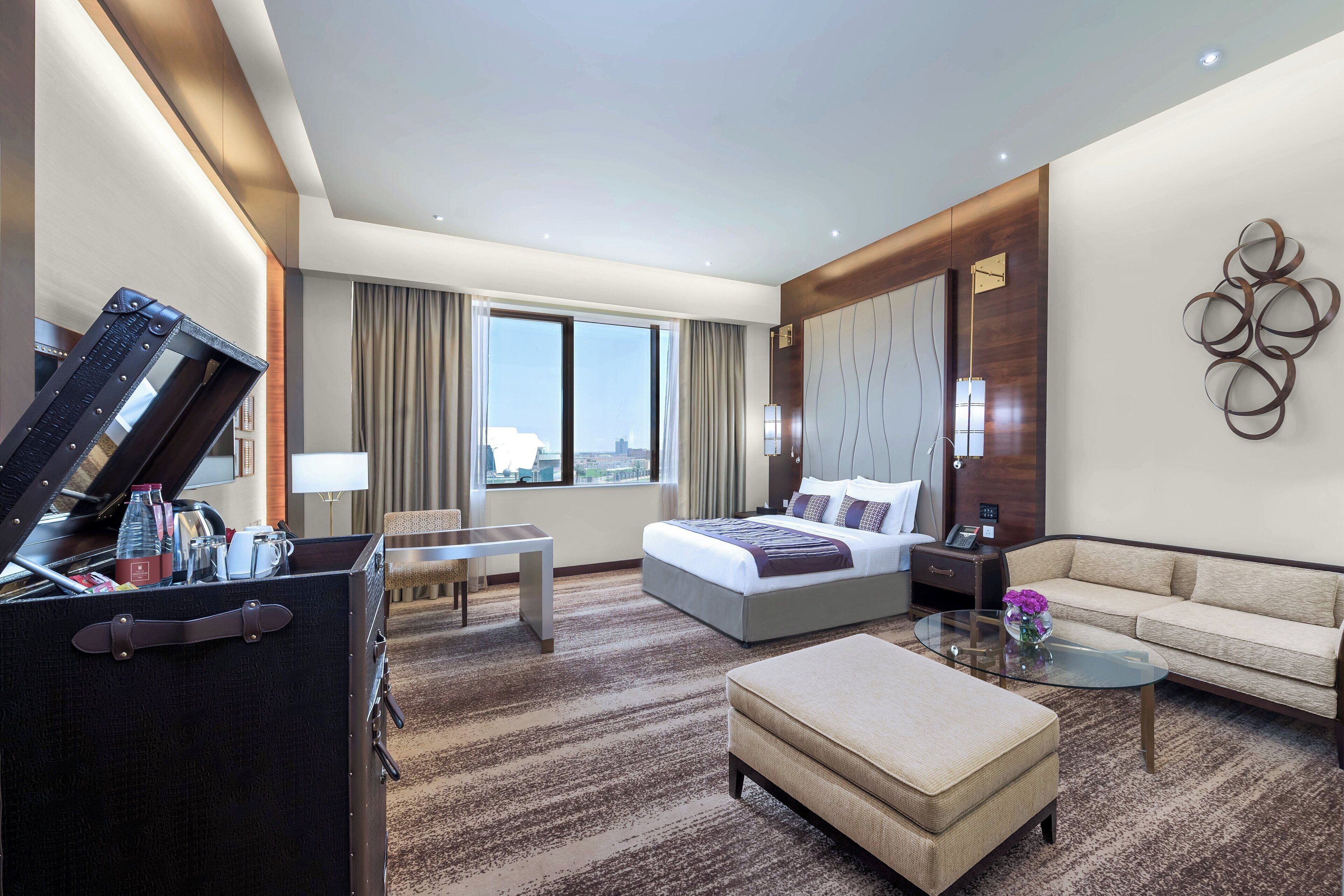 Quarto de hotel com cama, sofá, mesa de centro, escrivaninha e mala.