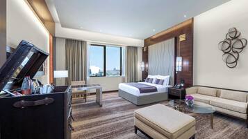 Quarto de hotel com cama, sofá, mesa de centro, escrivaninha e mala.