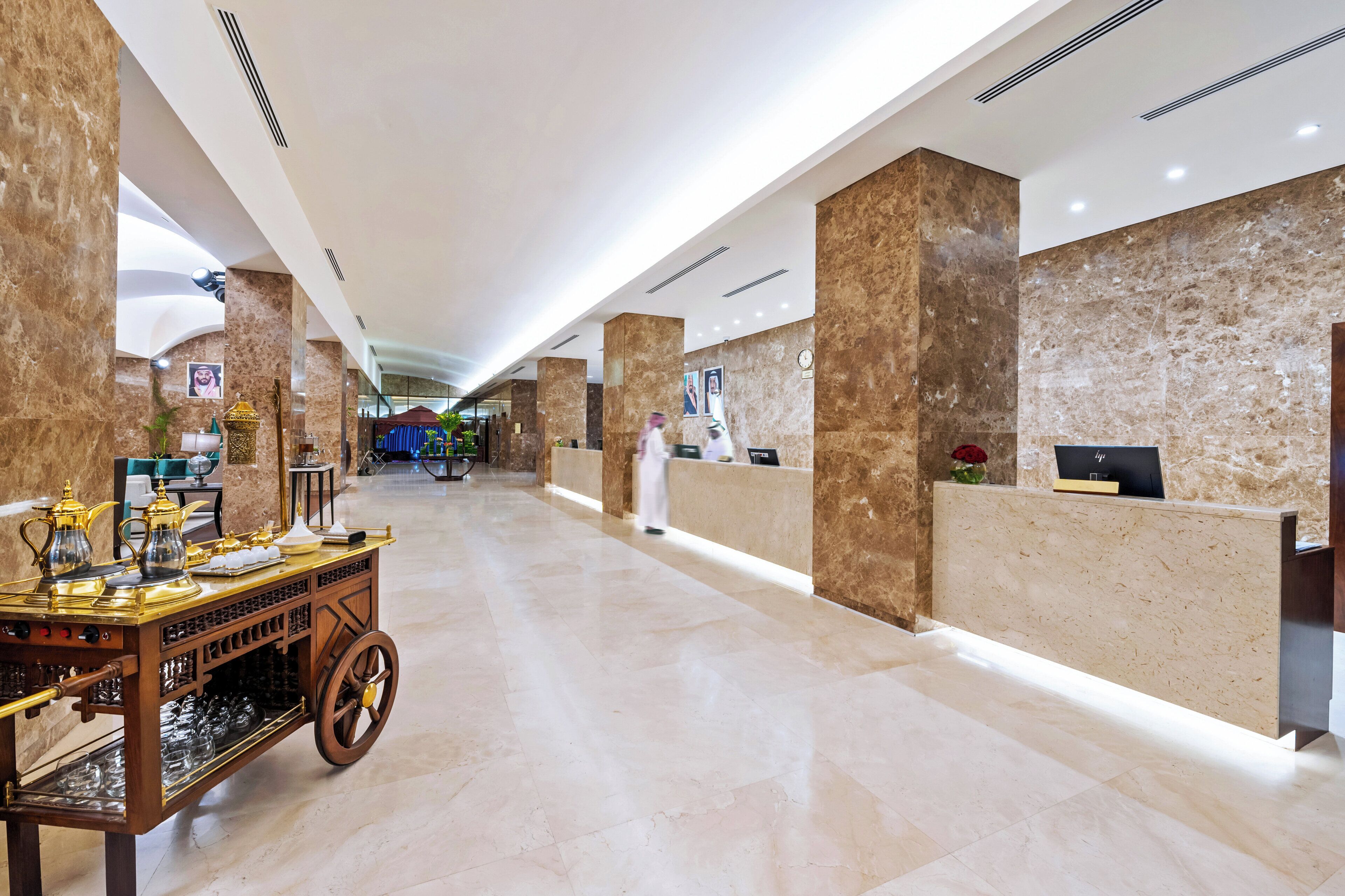 Um hall de hotel com colunas de mármore, um balcão de recepção e um carrinho de café tradicional.