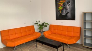 Uma sala de estar com dois sofás laranja, uma mesa de centro preta, uma planta em vaso e um quadro na parede.