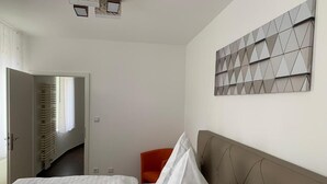 Quarto com cama, cabeceira, uma obra de arte na parede e porta que dá para um corredor.