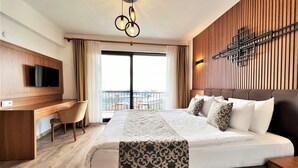 Quarto de hotel com uma cama grande, uma mesa, uma televisão e uma varanda com vista.