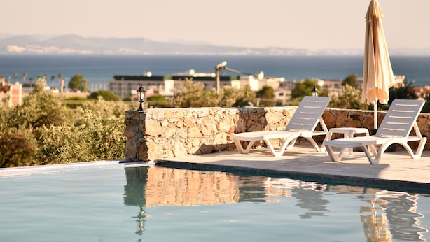 Piscina com espreguiçadeiras e um guarda-sol, com vista para a paisagem urbana e o mar.