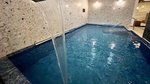 Piscina interior com recurso aquático, paredes revestidas e borda da piscina transparente.