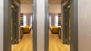 Um corredor com espelhos que leva a um quarto, com cama, mesa de cabeceira e cortinas.