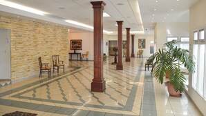 Um hall amplo com piso estampado, colunas de madeira e uma grande planta em vaso.