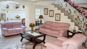 Uma sala de estar espaçosa com dois sofás de couro rosa, uma mesa de centro de madeira e um lance de escadas decorado com flores cor-de-rosa.