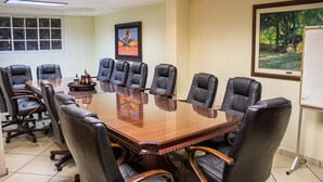 Uma sala de conferências com uma grande mesa de madeira rodeada por cadeiras de couro, um quadro branco e obras de arte emolduradas nas paredes.