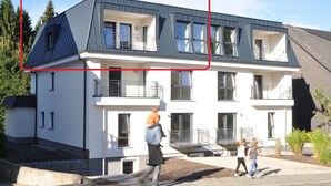 Um edifício residencial moderno de dois andares, com varandas, telhado inclinado e calçada pavimentada.