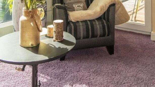 Quarto com poltrona listrada, uma mesa redonda pequena com um vaso de flores e vista para a varanda.