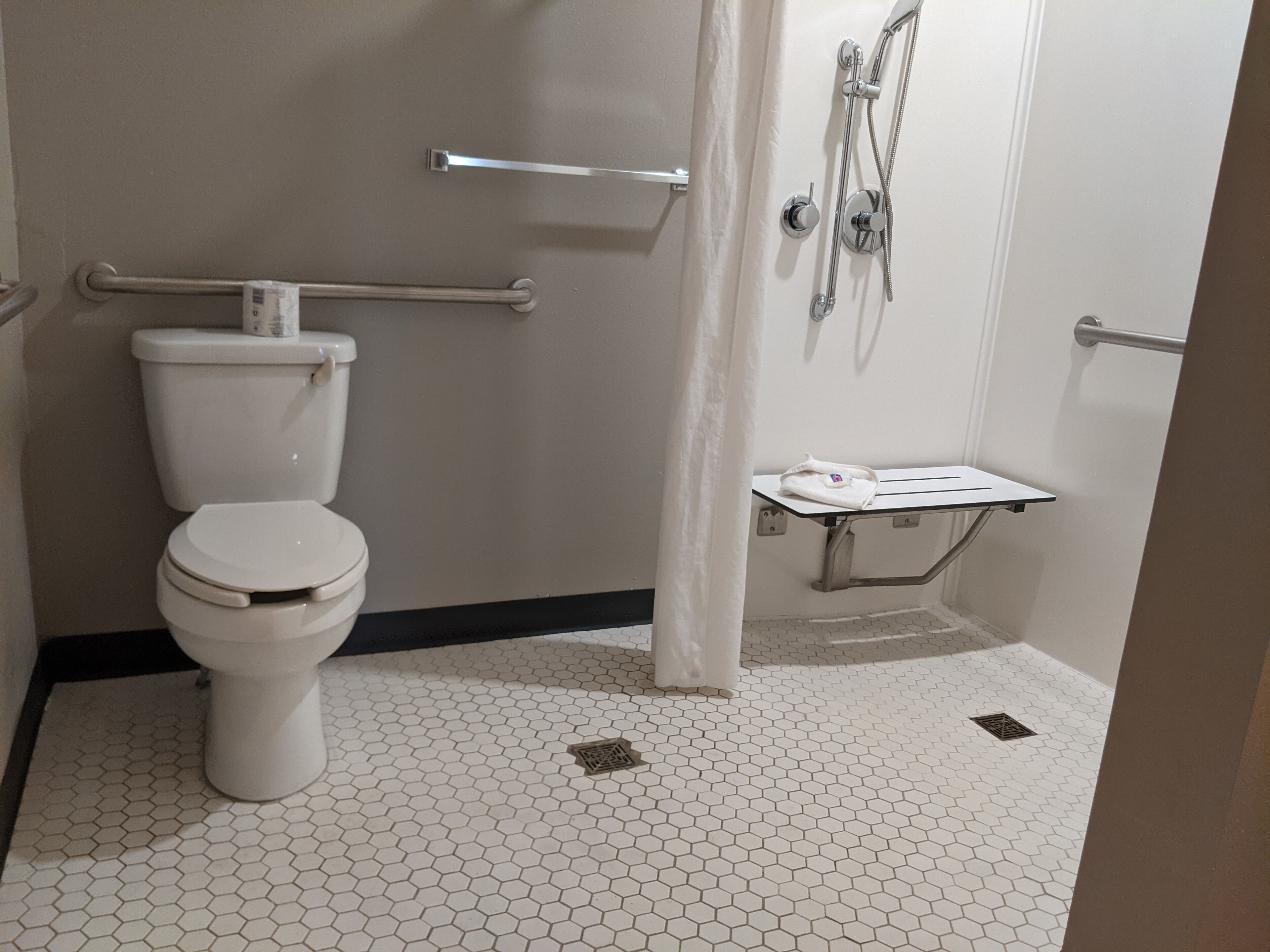 Uma casa de banho com sanita, zona de duche e uma pequena prateleira com uma toalha.