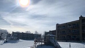 Uma área externa nevada com um edifício que possui várias varandas e um espaço coberto para sentar.