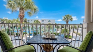 Varanda com mesa posta para dois, vista para uma piscina e rua com palmeiras e edifícios.