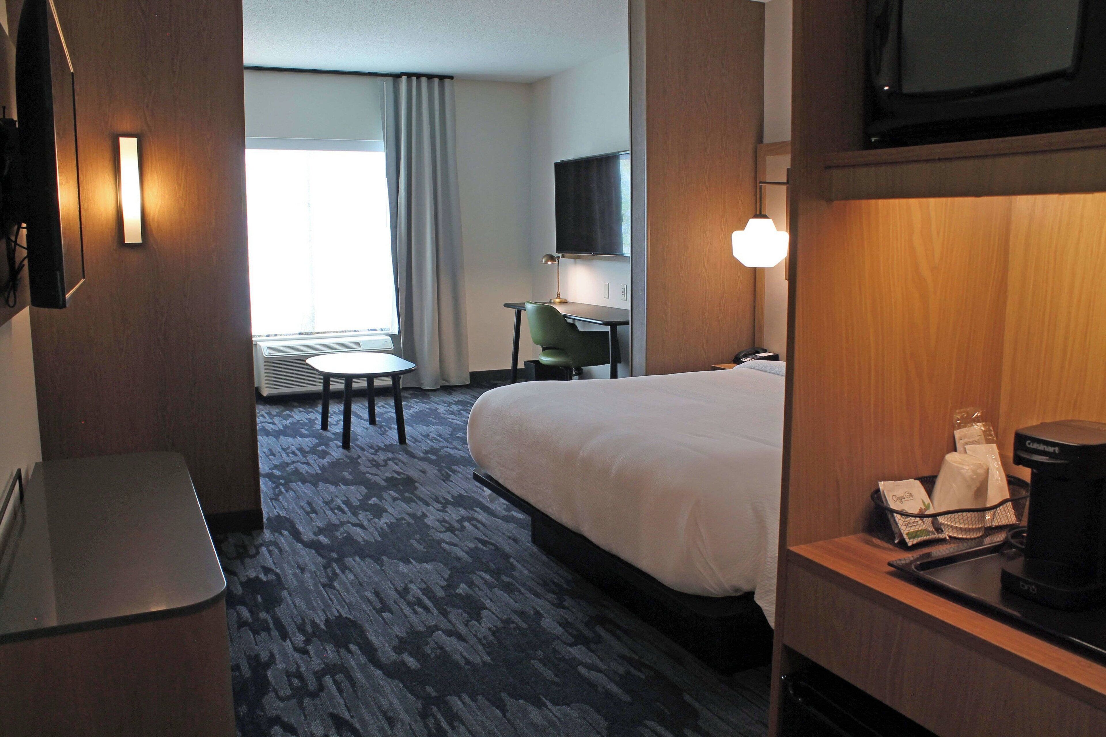 Quarto de hotel com cama, escrivaninha, cadeira, televisão e máquina de café.