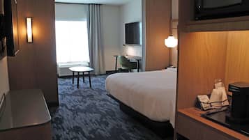 Quarto de hotel com cama, escrivaninha, cadeira, televisão e máquina de café.