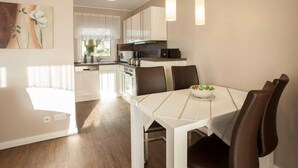 Cozinha moderna com armários brancos, mesa de jantar com cadeiras, luminárias pendentes e vista para o exterior.