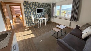 Uma sala de estar moderna com sofá, televisão, uma mesinha e uma janela com cortinas.
