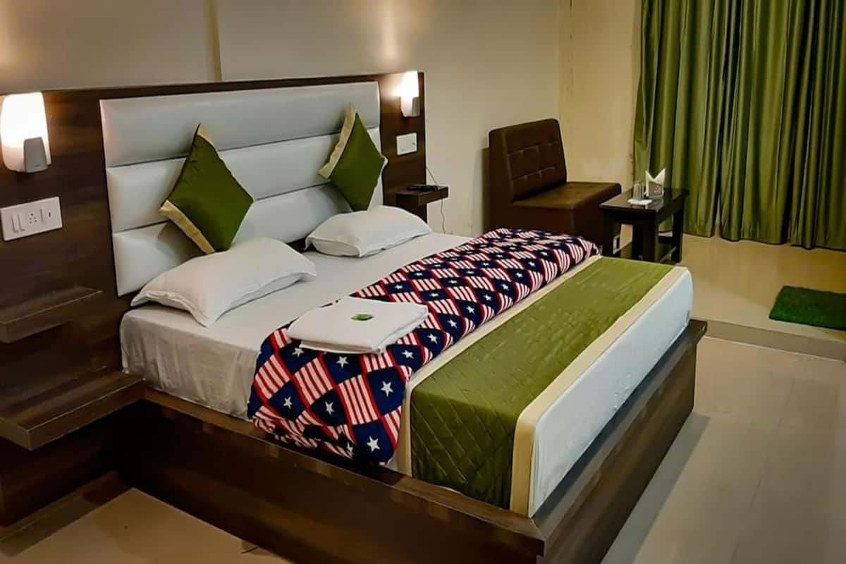 Quarto de hotel com uma cama grande, uma mesa de cabeceira, uma cadeira e uma pequena mesa com abajur.