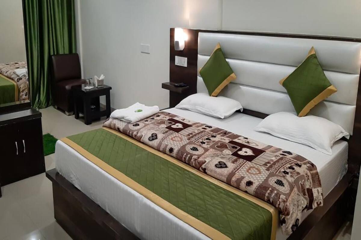 Quarto de hotel bem arrumado, com uma cama grande, uma mesinha de cabeceira, uma cadeira e um armário.