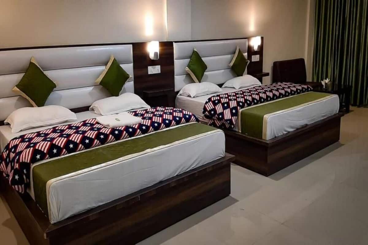 Quarto de hotel com duas camas, cada uma com cabeceira, almofadas e manta.