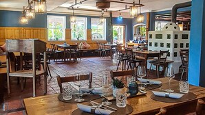 Um restaurante com mesas e cadeiras de madeira, e luminárias pendentes.