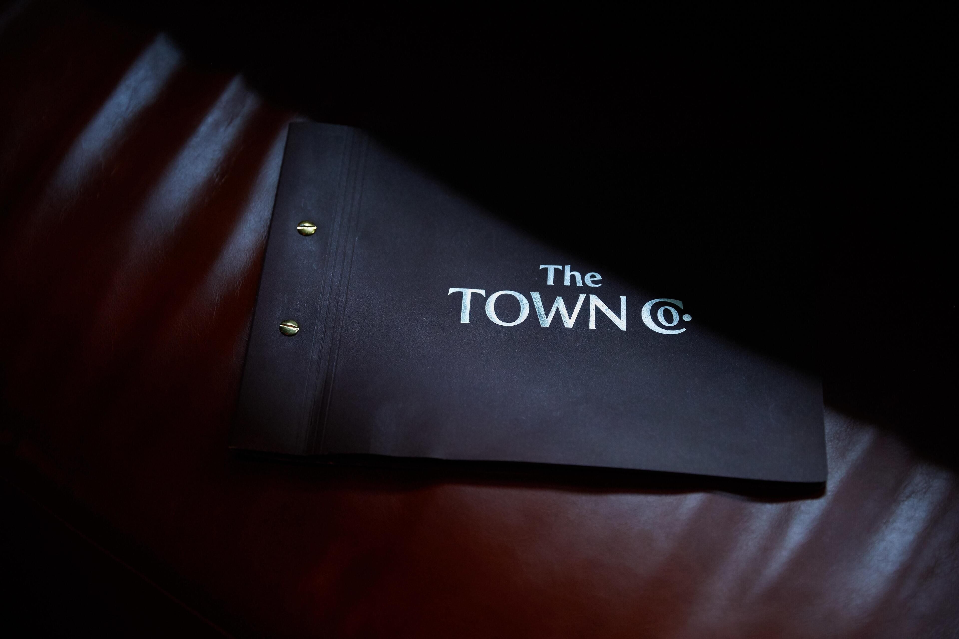 Uma pasta preta com o texto 'The TOWN' e um símbolo, colocada sobre uma superfície escura.