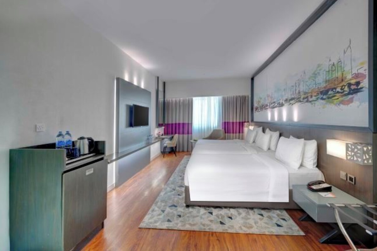 Quarto de hotel moderno com uma cama grande, uma mesa, uma TV e uma kitchenette.