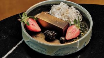 Uma tigela com sobremesa, morangos, um framboesa e um pedaço de chocolate, sobre superfície escura.