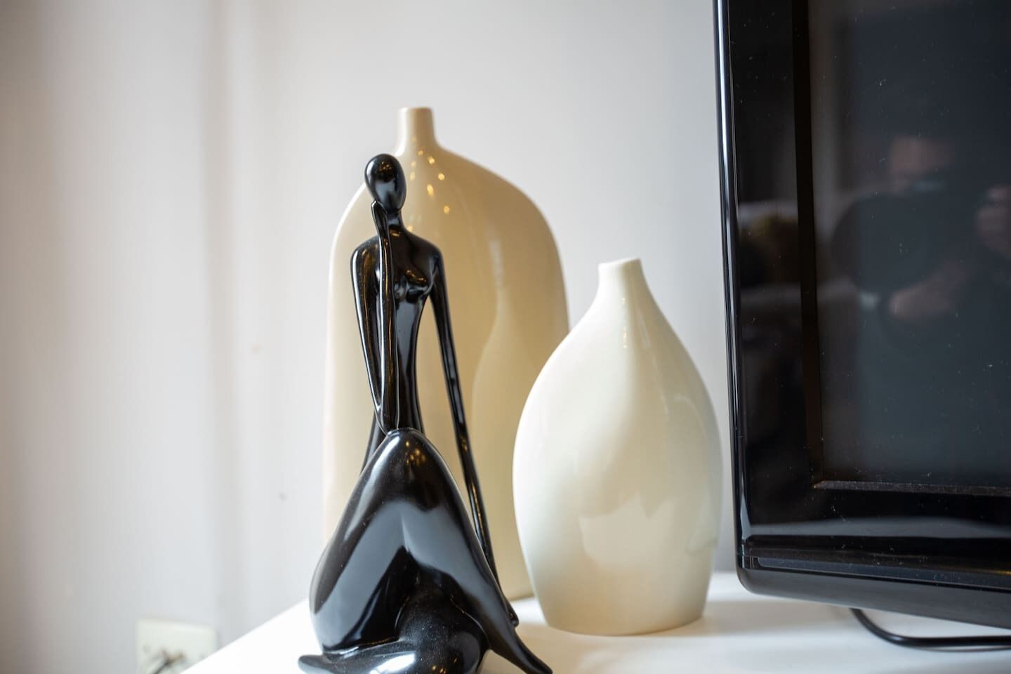 Uma mesa com uma estatueta, um vaso branco e um monitor de computador.