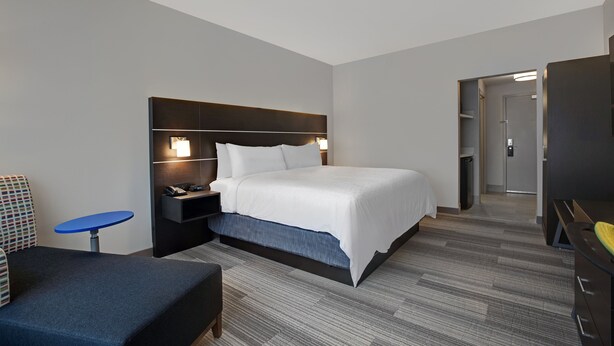 Quarto de hotel com cama, mesa de cabeceira, luminária e escrivaninha com cadeira.