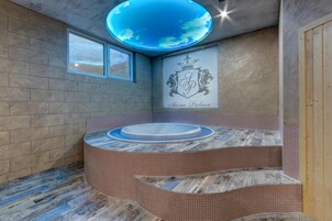 Uma área de spa com hidromassagem, teto com design inspirado no céu e parede com emblema de brasão.