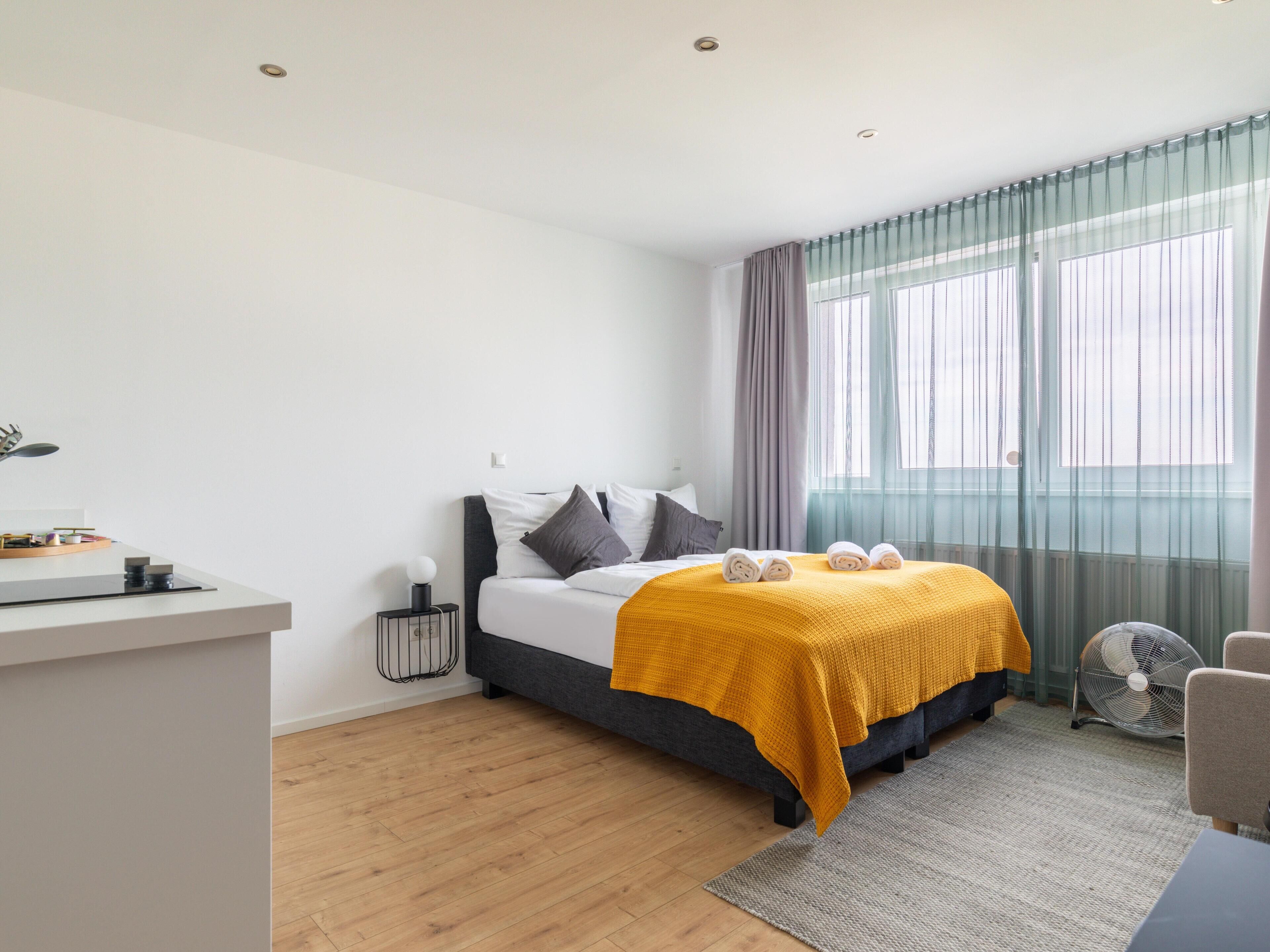 Quarto de hotel moderno com cama, escrivaninha e janela com cortinas.