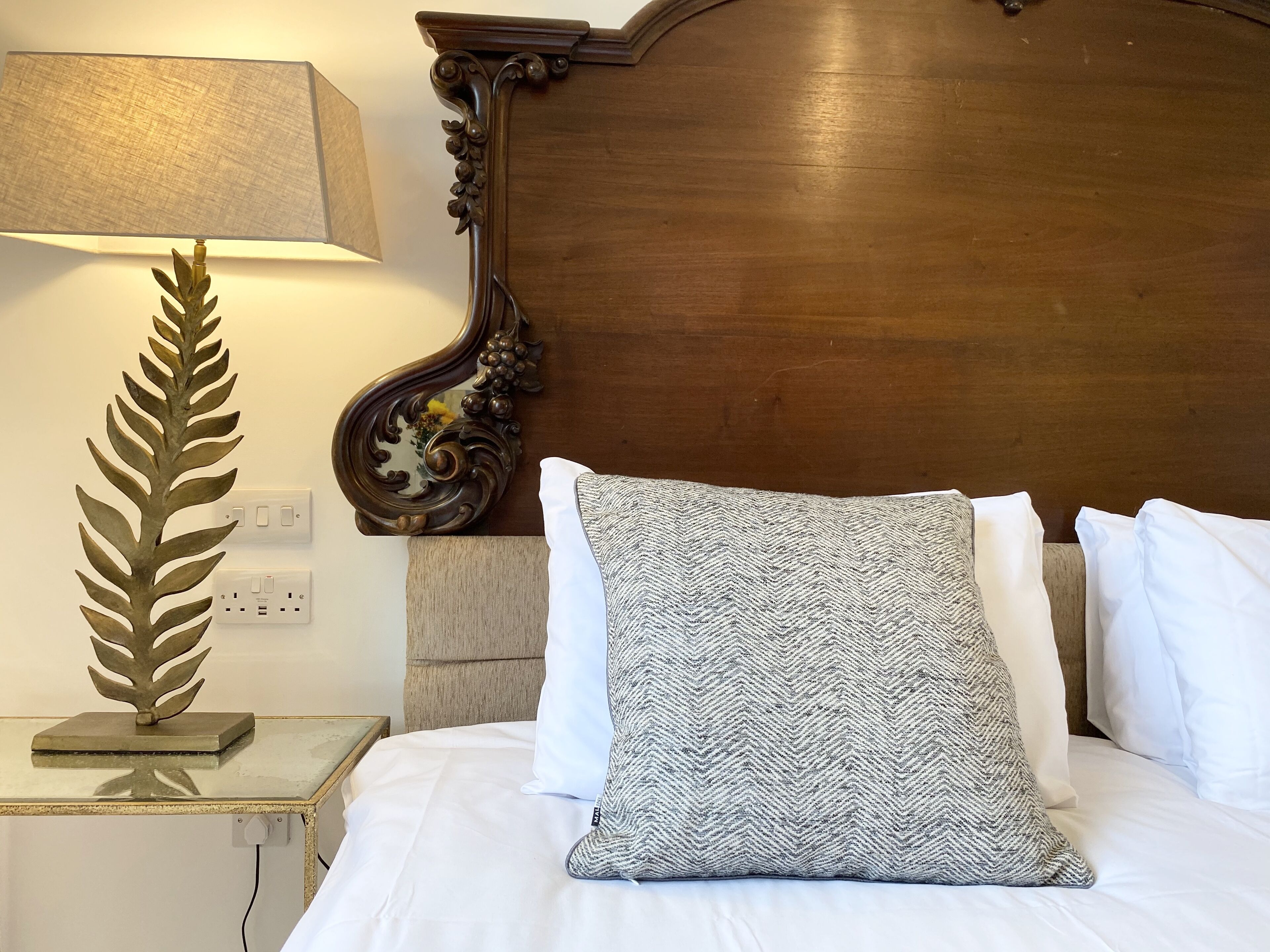 Cama bem arrumada com lençóis brancos, almofada estampada e cabeceira de madeira.
