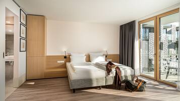 Quarto de hotel moderno com uma cama grande, guarda-roupa, banheiro e varanda com vista para a cidade.