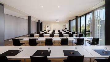 Uma sala de conferências moderna com várias mesas e cadeiras, janelas amplas e uma tela de projetor.
