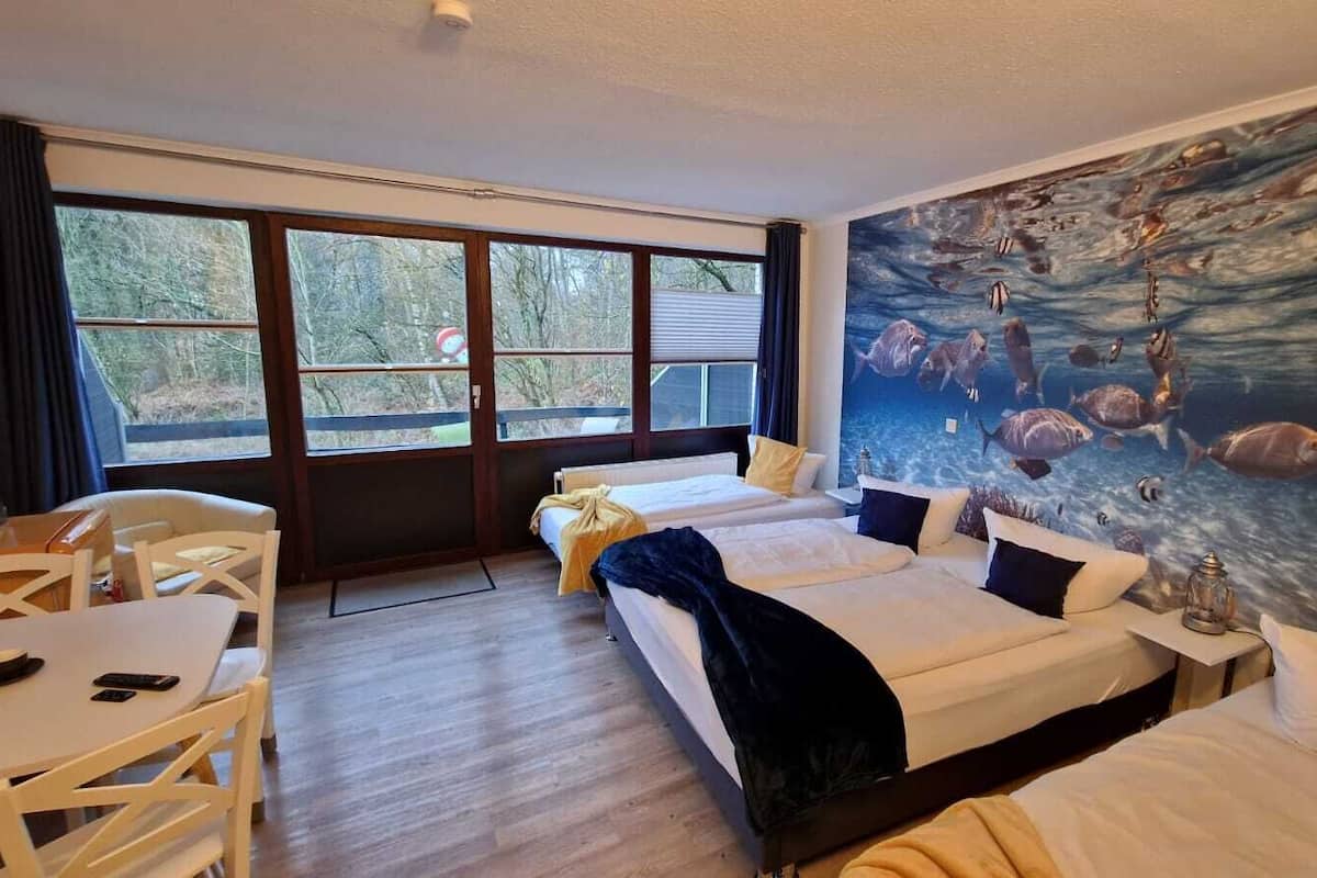 Quarto de hotel com duas camas, uma mesa de jantar e um grande mural de peixes na parede.