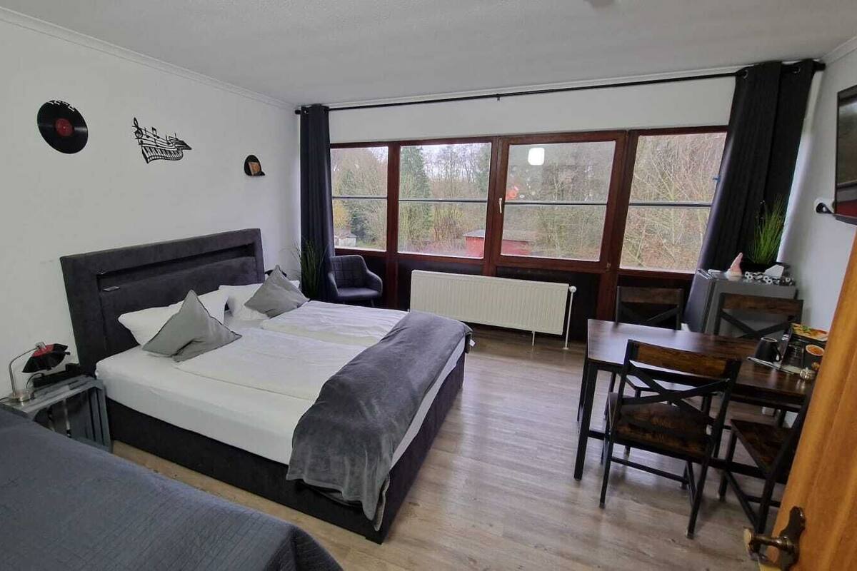 Quarto com cama, escrivaninha e cadeira. Há janelas e um radiador.