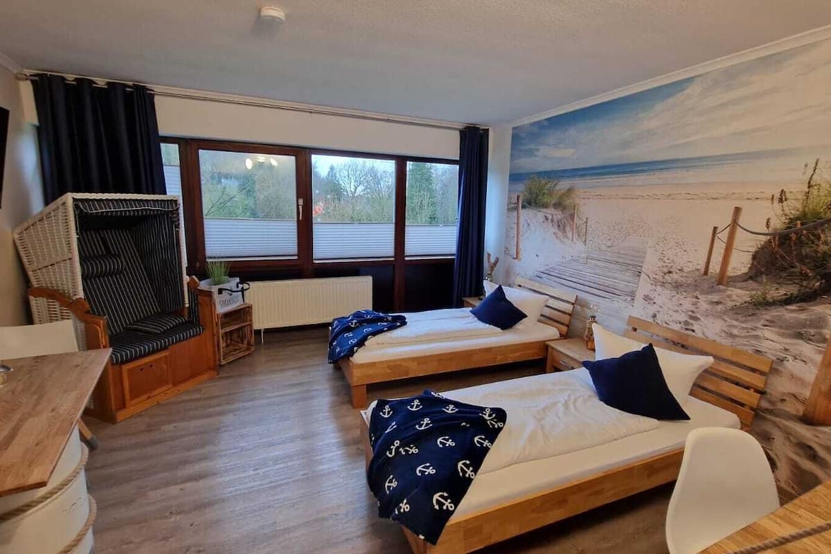 Quarto com três camas de madeira, televisão, uma cadeira e uma grande janela com um mural de praia.