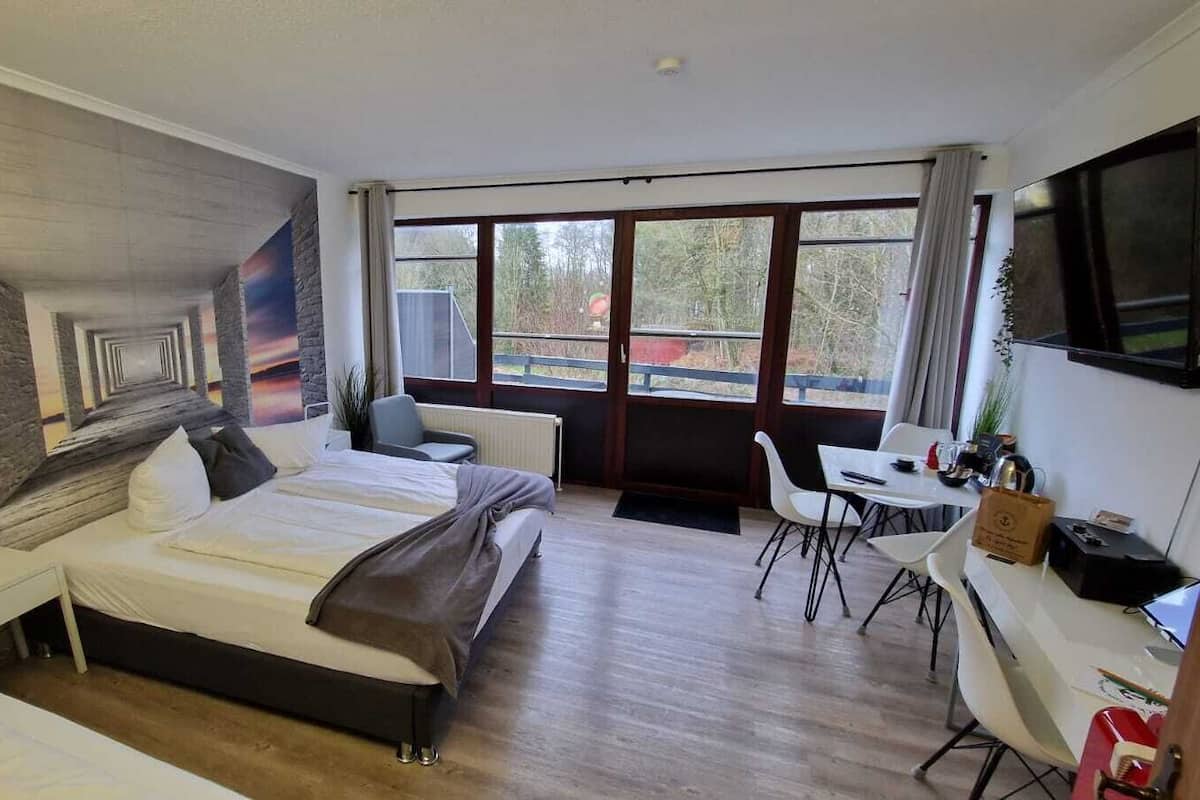 Quarto de hotel moderno com uma cama grande, uma mesa e uma cadeira. Há vista para o exterior por grandes janelas.