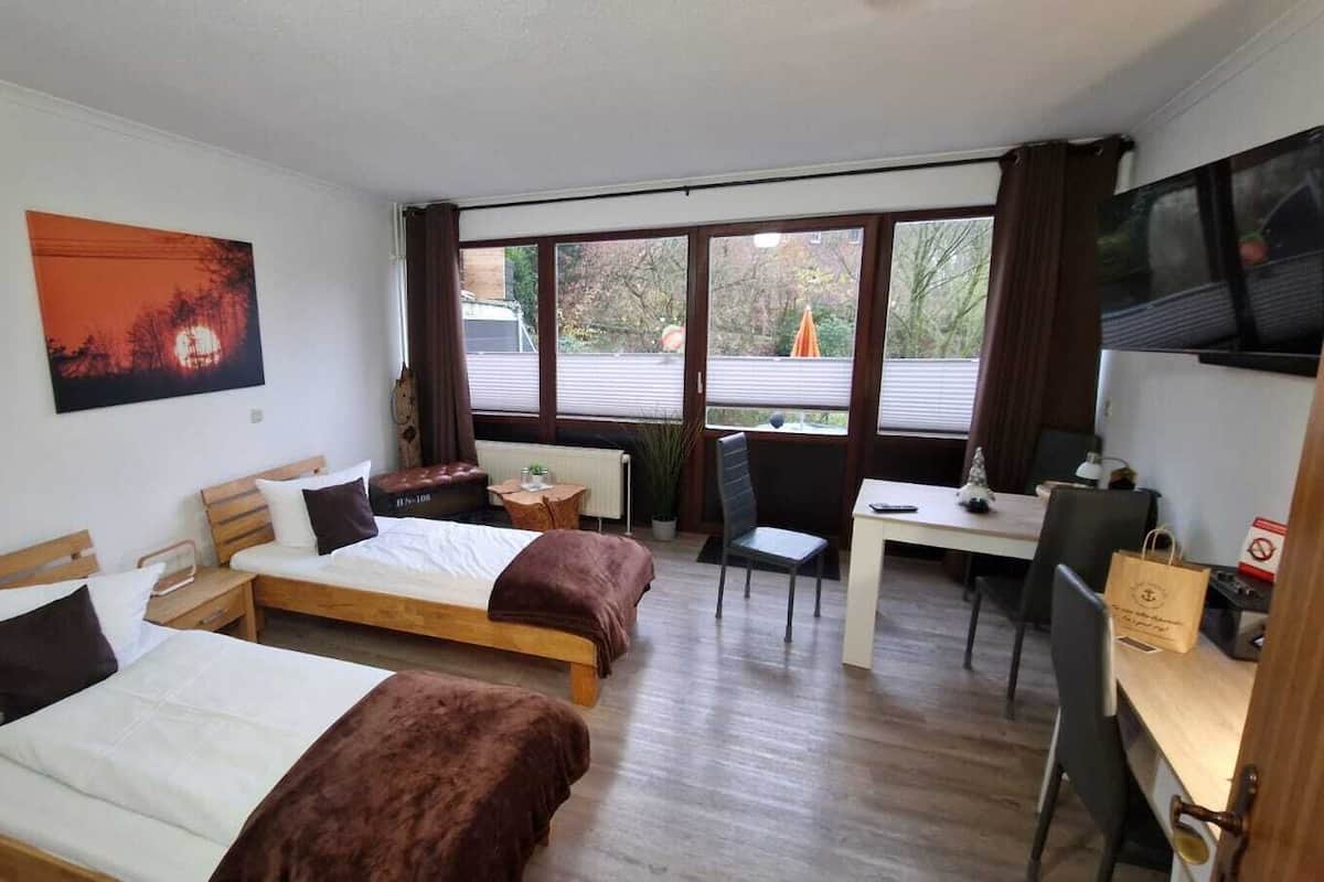 Quarto de hotel com duas camas, uma escrivaninha, uma cadeira, uma televisão e janela com vista para o exterior.