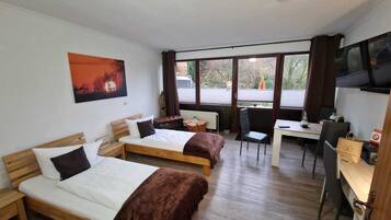 Quarto de hotel com duas camas, uma escrivaninha, uma cadeira, uma televisão e janela com vista para o exterior.
